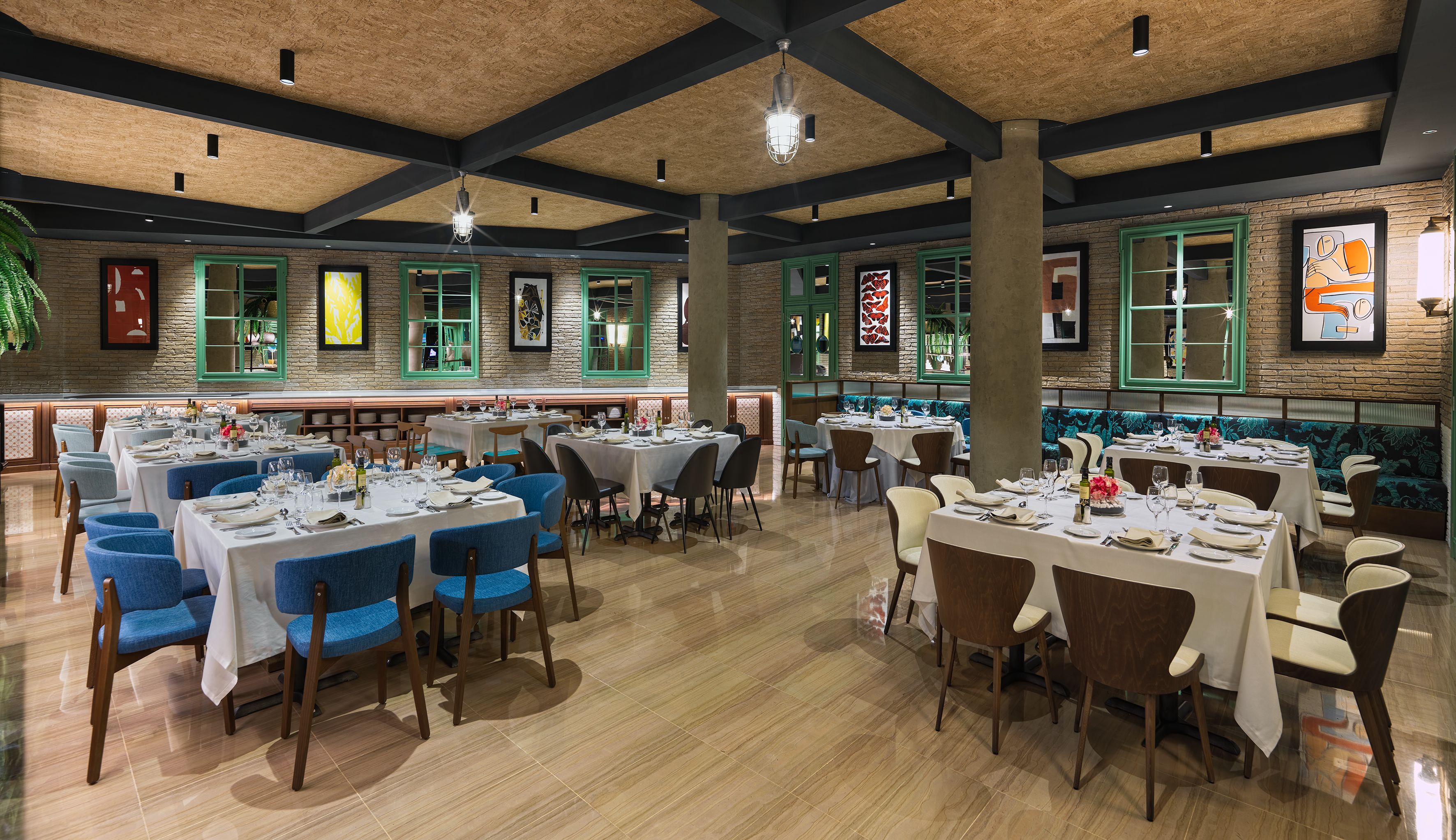 Um restaurante com várias mesas e cadeiras, piso de madeira e janelas com moldura verde.