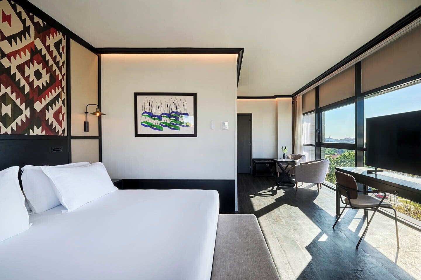 Quarto de hotel moderno com uma cama grande, uma escrivaninha e uma televisão.
