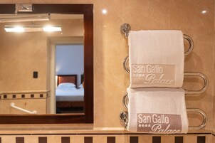 Um banheiro com espelho, porta-toalhas com duas toalhas e porta que dá para um quarto.