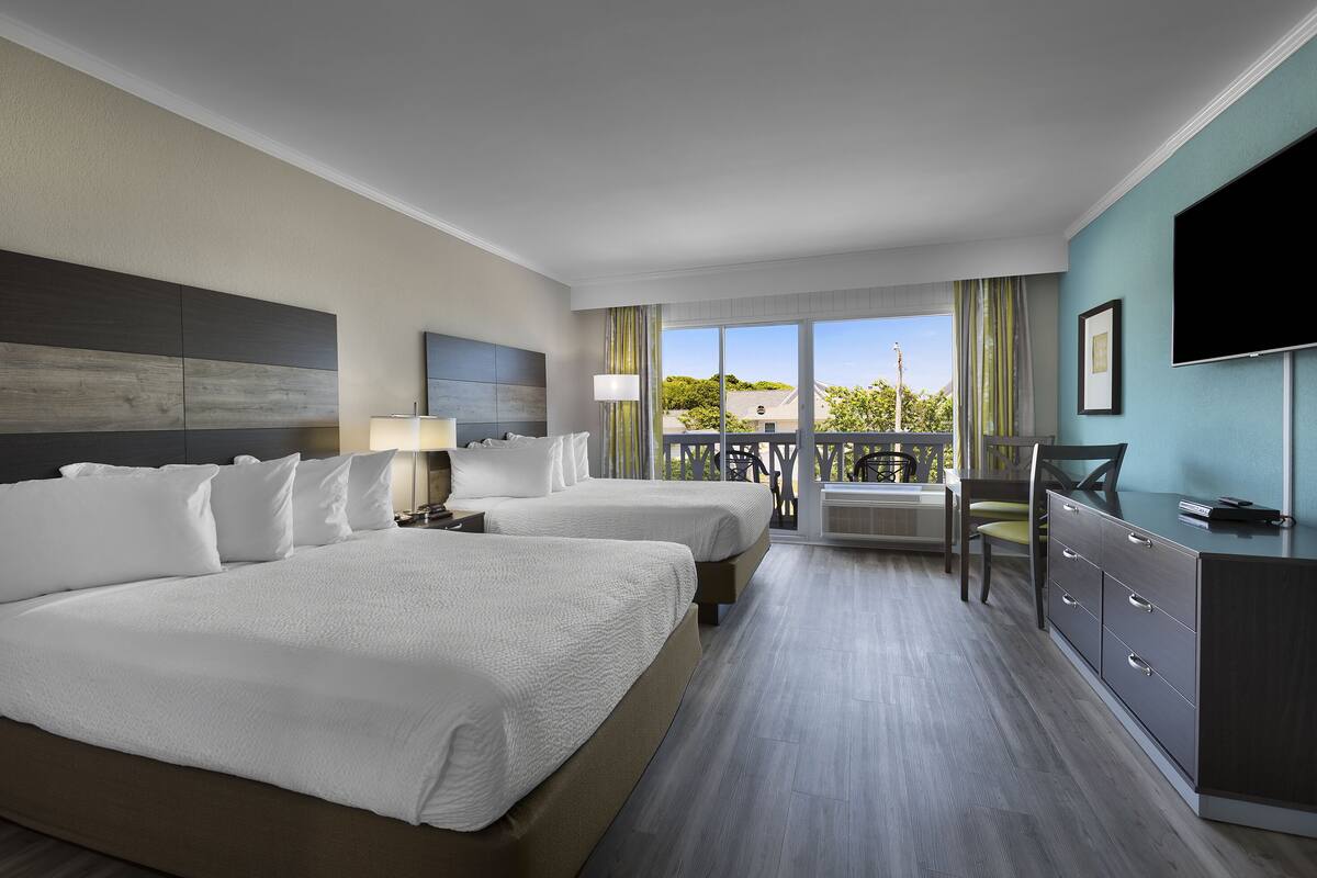 Quarto de hotel com duas camas, uma escrivaninha, televisão e varanda com vista.