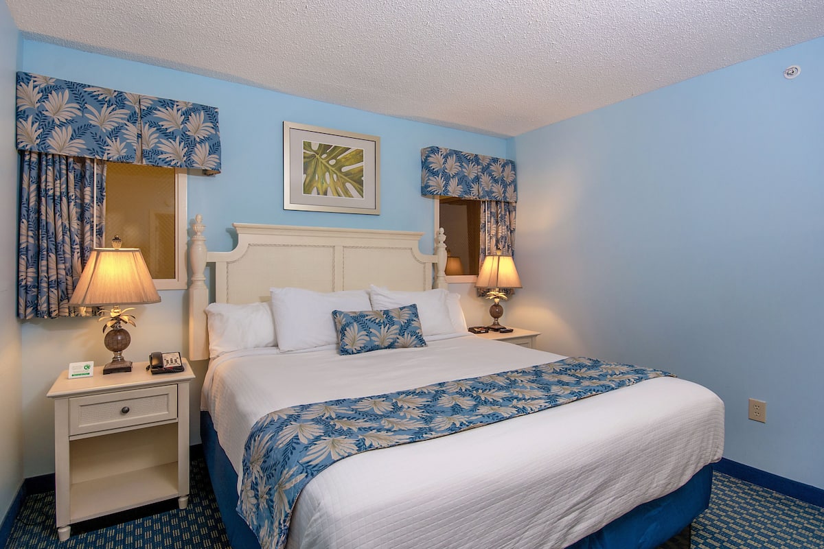 Quarto de hotel com uma cama grande, duas mesas de cabeceira e um espelho fixado na parede.