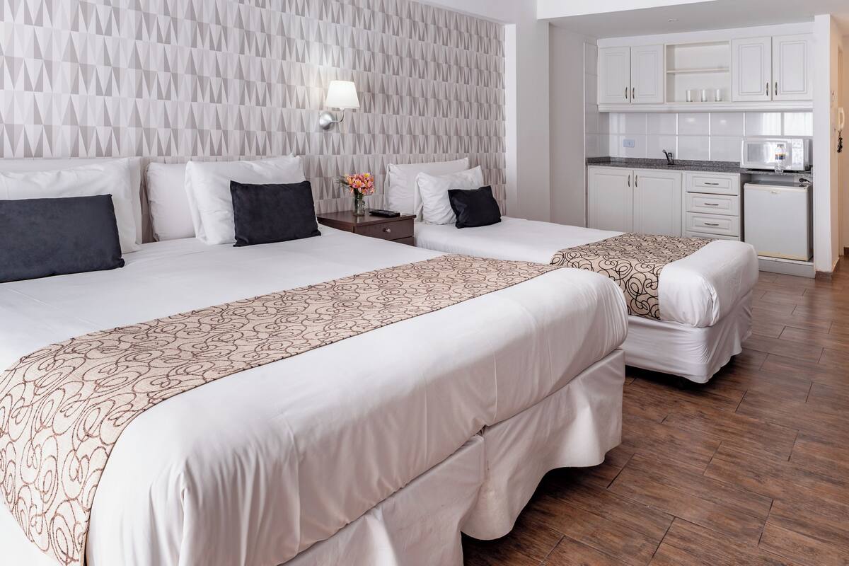 Quarto de hotel com duas camas, uma cozinha compacta e parede estampada.