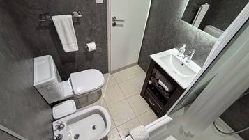 Casa de banho compacta com sanita, bidé, lavatório e espelho.