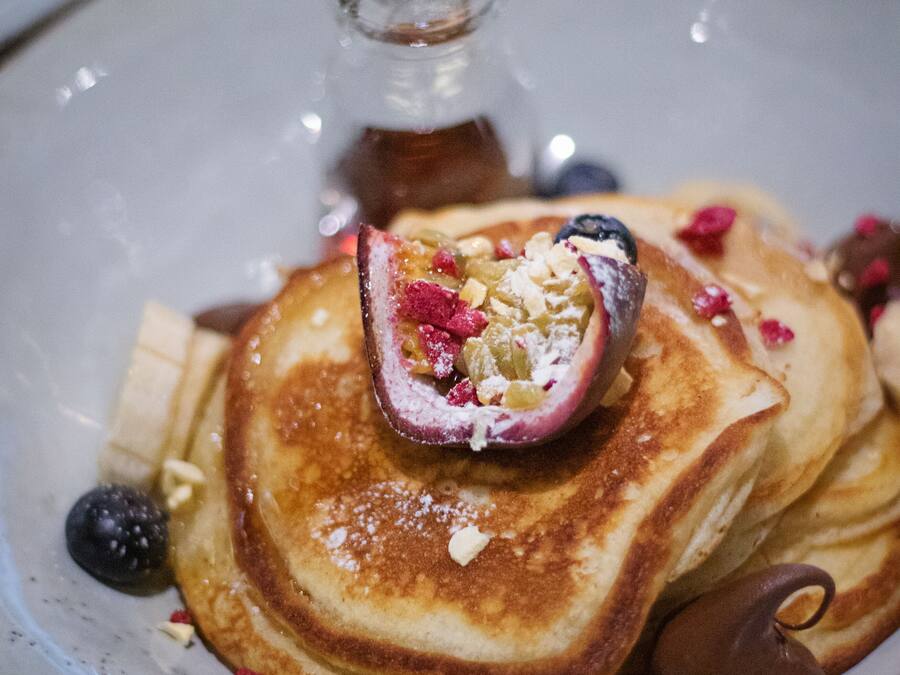 Um prato com panquecas cobertas de frutas e um copo de um líquido castanho, provavelmente xarope.