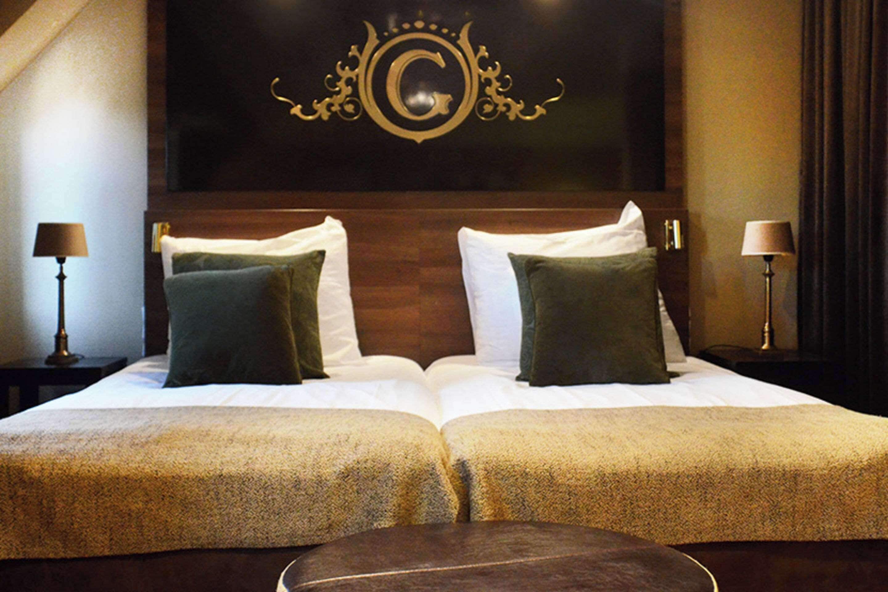 Uma cama de casal com duas almofadas, uma mesa de cabeceira com abajur e um objeto decorativo na parede.