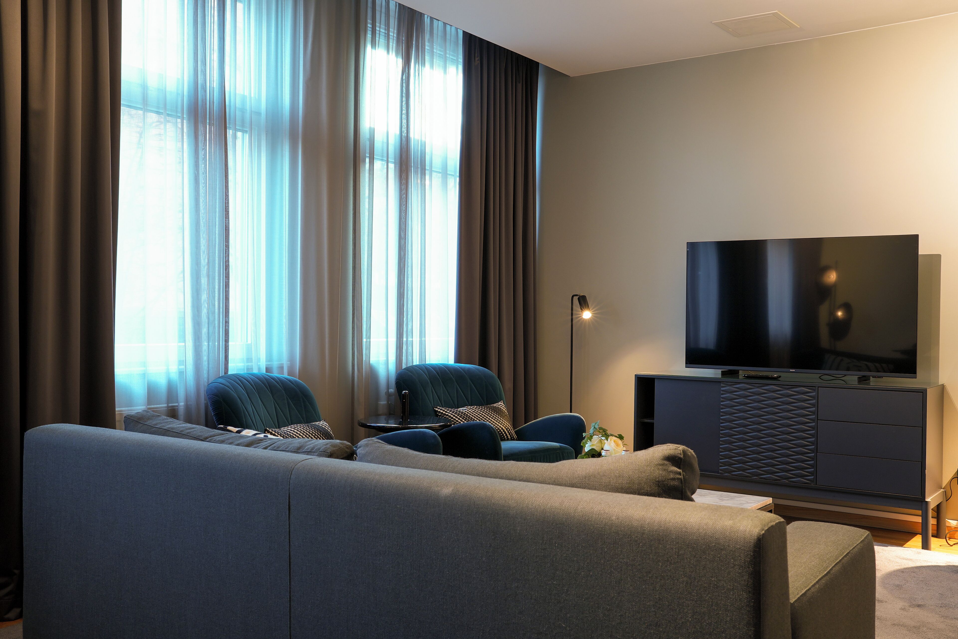 Uma sala de estar moderna com um sofá grande, duas poltronas, uma televisão de tela plana e um aparador.