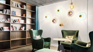 Uma biblioteca moderna com poltronas verdes, uma mesa redonda e uma estante repleta de livros.