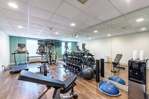 Uma academia com equipamentos de ginástica, esteira, remo e bebedouro.