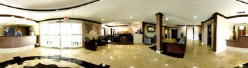 Um saguão de hotel com balcão de recepção, área de estar e uma tela de televisão.
