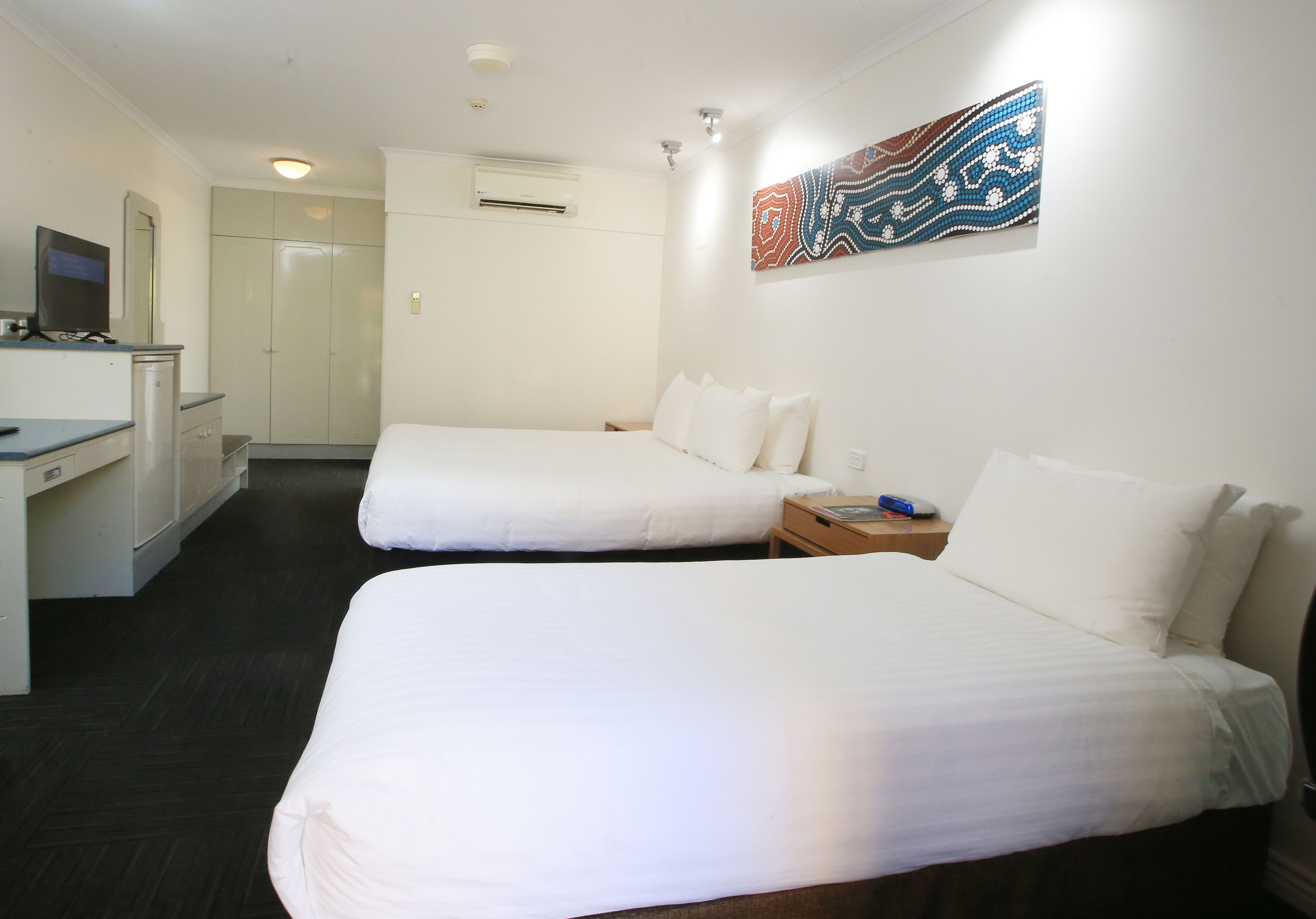 Quarto de hotel com duas camas, uma escrivaninha, uma televisão e um guarda-roupa.