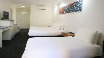 Quarto de hotel com duas camas, uma escrivaninha, uma televisão e um guarda-roupa.