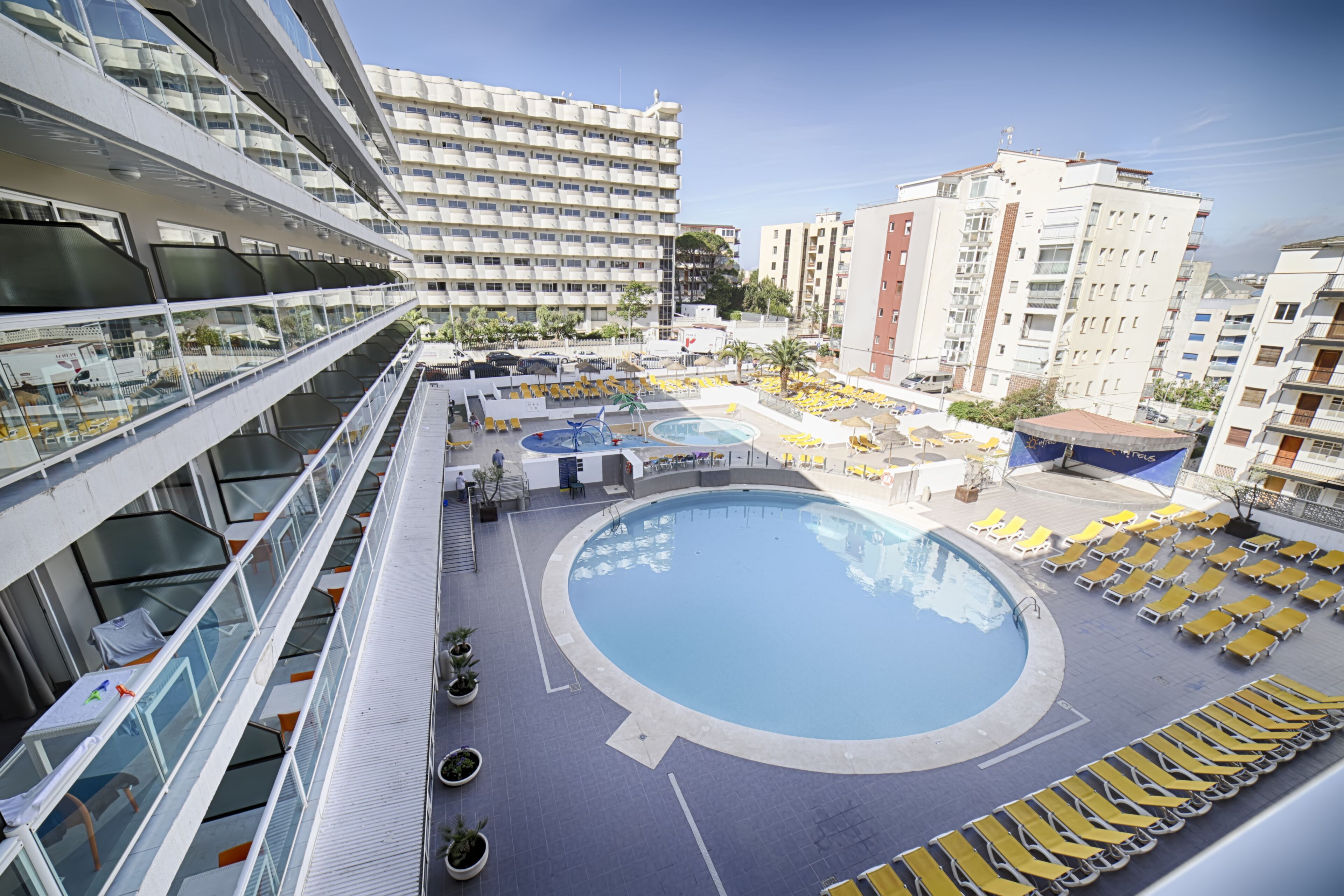 Piscina no terraço com espreguiçadeiras e um tobogã, cercada por edifícios modernos.