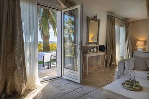 Quarto de hotel com porta de vidro deslizante para área externa com mesa e cadeiras, pequena escrivaninha com espelho e sofá.