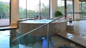 Uma piscina interior moderna com piso de vidro, uma banheira de hidromassagem e uma escadaria que dá para um terraço.