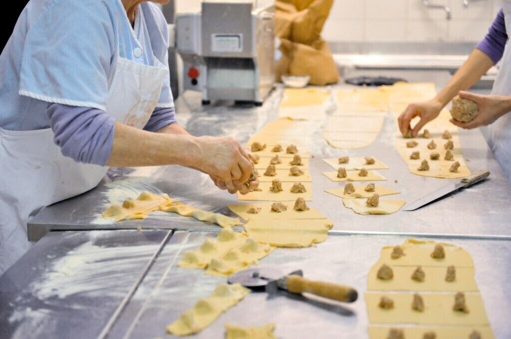 Uma cozinha com chefs preparando alimentos, com massa e ingredientes sobre o balcão.