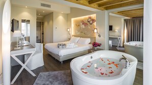 Quarto de hotel moderno com uma cama grande, uma escrivaninha, uma área de estar, uma banheira com pétalas de rosa e uma parede com um mural de borboletas.