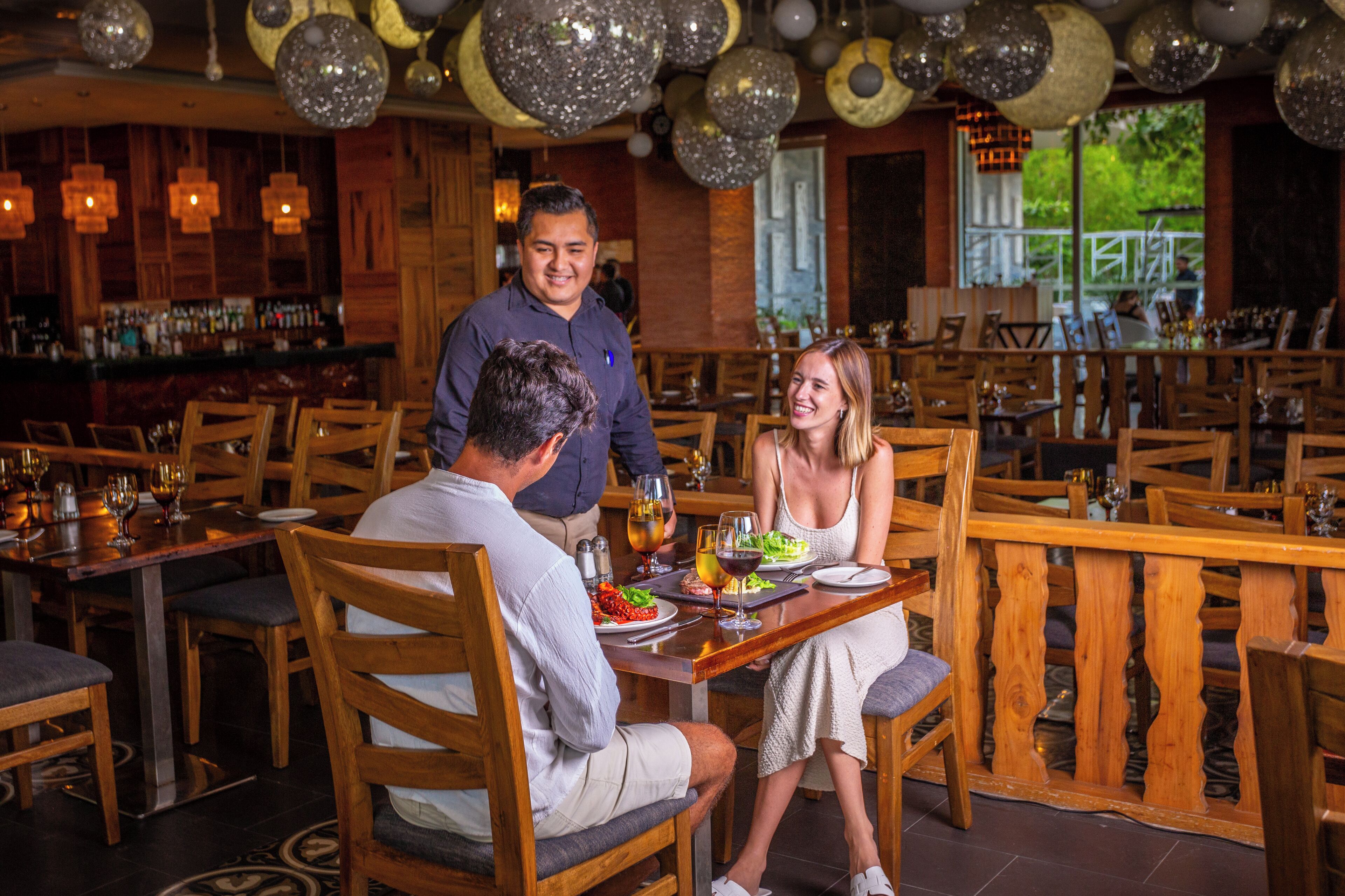 Restaurante com móveis de madeira, área de bar e bolas de discoteca penduradas.