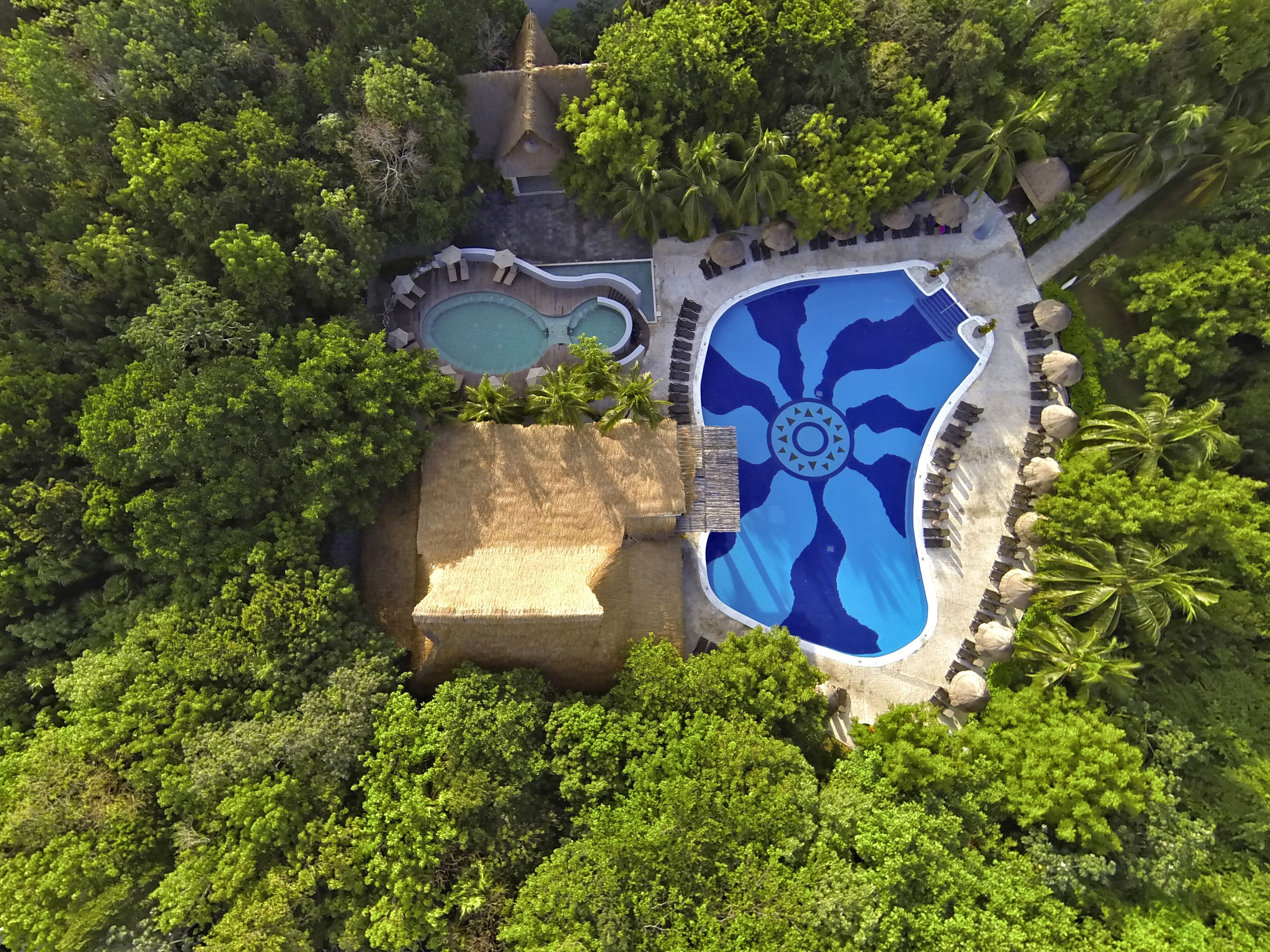 Vista aérea de um resort com duas piscinas cercadas por vegetação exuberante e palmeiras.