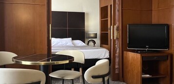Quarto de hotel com uma cama, televisão, escrivaninha e duas cadeiras.