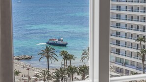 Vista de uma praia com barco, palmeiras e um hotel.