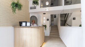 Um balcão de recepção moderno com acabamento em madeira, um recepcionista e uma escadaria que leva a um andar superior.