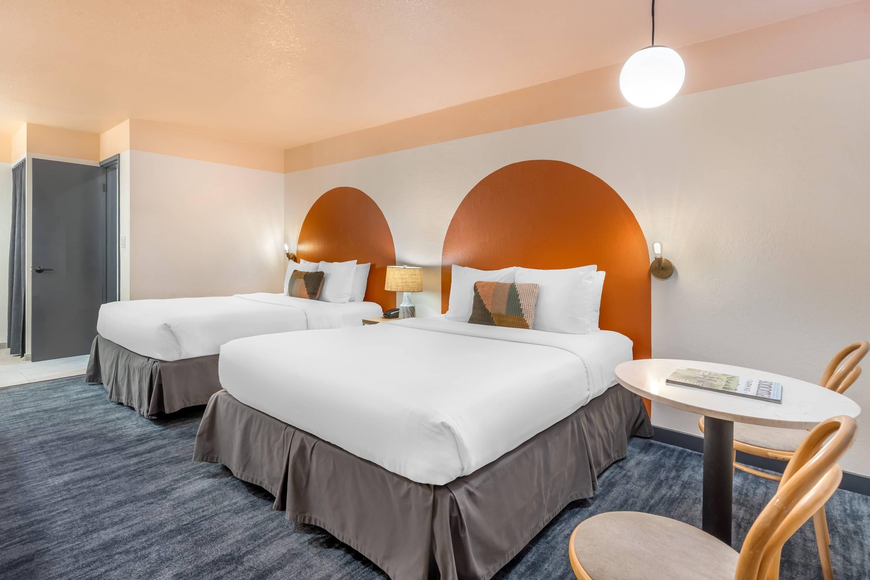 Quarto de hotel com duas camas, uma mesa redonda e uma cadeira.