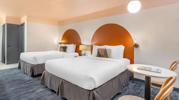 Quarto de hotel com duas camas, uma mesa redonda e uma cadeira.