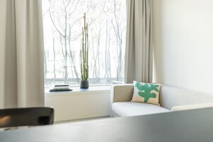 Uma sala de estar moderna com um sofá, uma mesinha e uma janela com vista para árvores.