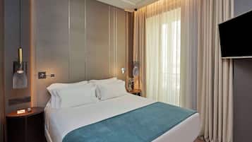 Quarto de hotel com cama, televisão presa na parede e mesa de cabeceira com abajur.