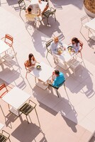 Um café ao ar livre com várias mesas e cadeiras, dispostas em um espaço amplo.