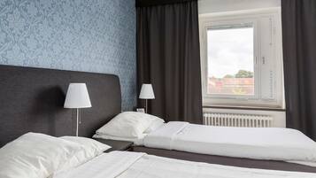 Quarto de hotel com duas camas, uma cabeceira escura, uma janela com cortinas e uma parede com padrão azul.