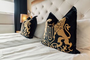 Cama com roupa de cama branca e duas almofadas pretas com bordado dourado.