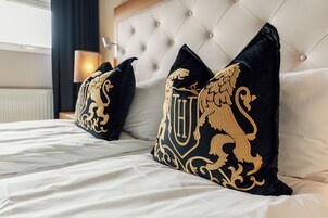 Cama com roupa de cama branca e duas almofadas pretas com bordado dourado.