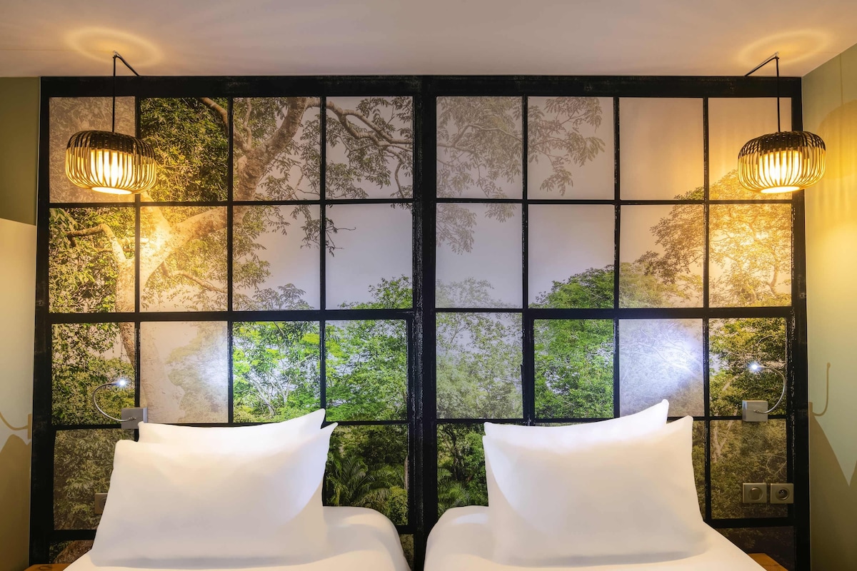 Quarto com duas camas, uma janela grande com vista para árvores e duas luminárias na parede.