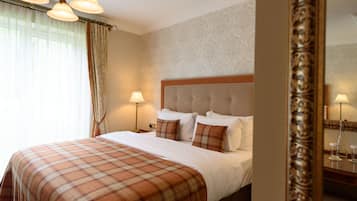 Quarto de hotel com uma cama grande, cabeceira, duas mesas de cabeceira com abajures, um espelho e uma janela com cortinas.