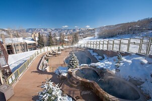 Área externa coberta de neve com hidromassagem, espaço para sentar e vista para montanhas.