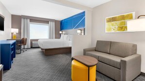 Quarto de hotel com cama, sofá, escrivaninha, cadeira, televisão e janela.