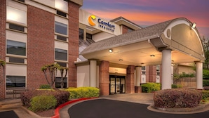 Um hotel Comfort Inn & Suites com fachada de tijolos, entrada coberta e céu claro.