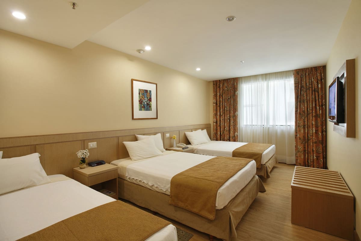 Quarto de hotel com três camas, televisão e janela com cortinas.
