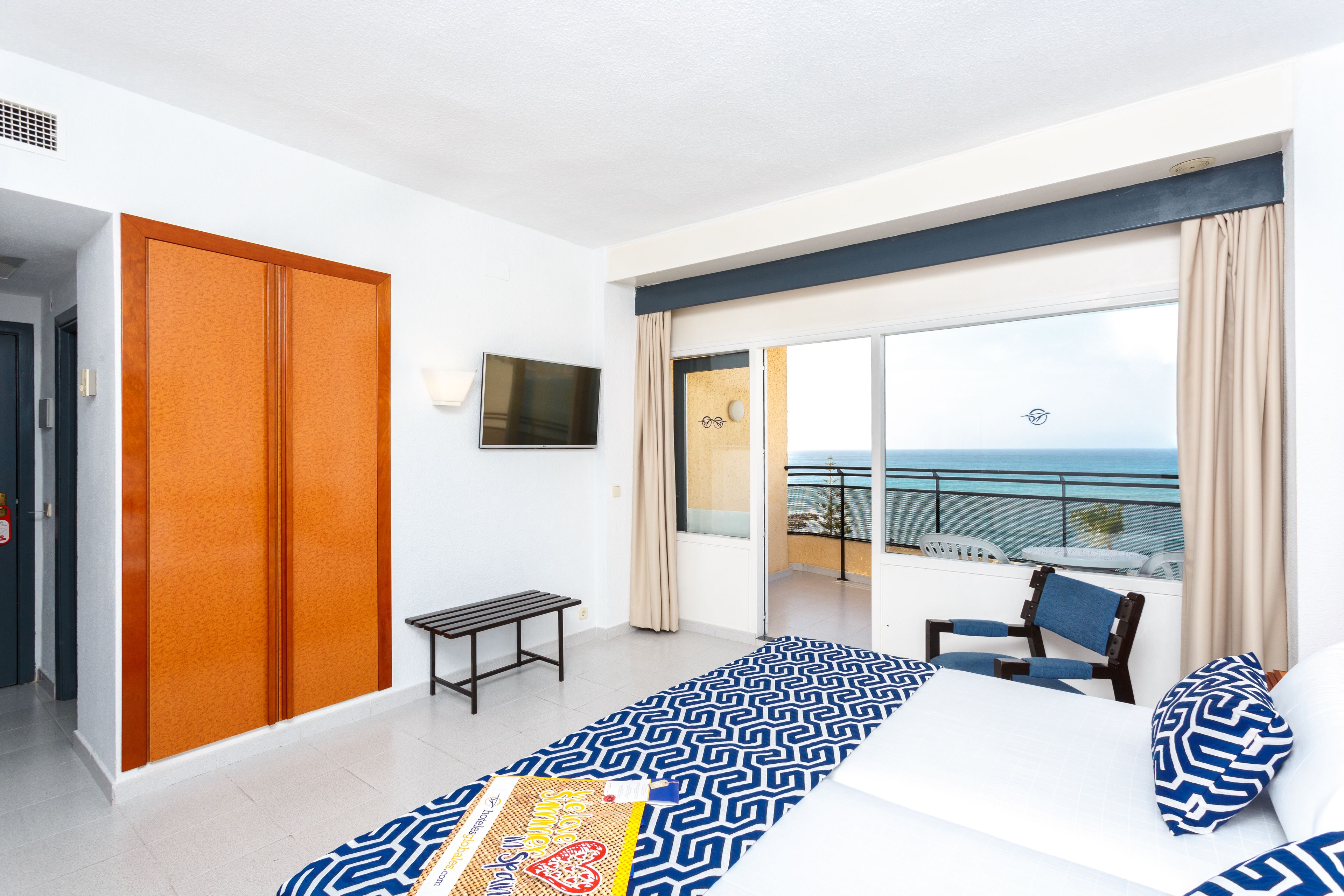 Quarto de hotel com cama, poltrona, televisão e varanda com vista para o mar.