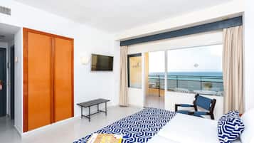 Quarto de hotel com cama, poltrona, televisão e varanda com vista para o mar.