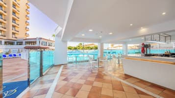 Um saguão de hotel com área de piscina, assentos e uma mesa de recepção.