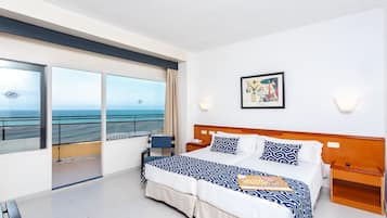 Quarto de hotel com cama grande, mesa de cabeceira, cadeira, janela com vista para o mar e quadro pendurado na parede.