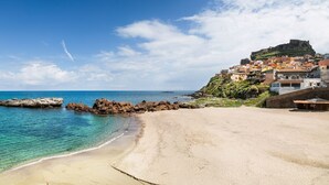 Uma vila costeira com uma praia arenosa, litoral rochoso e uma fortaleza histórica numa colina.