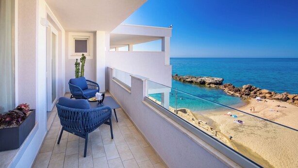 Uma varanda com vista para o mar, uma cadeira, uma mesa pequena e um vaso de planta.