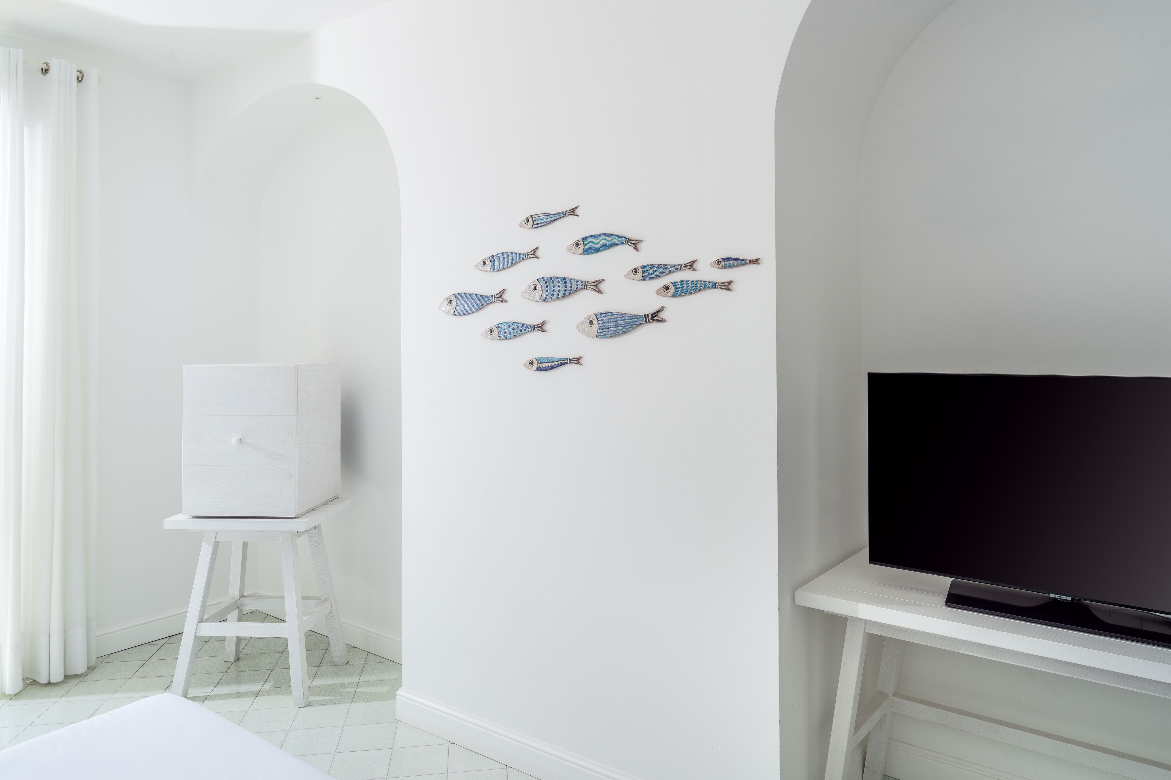 Um quarto com parede branca, uma TV de tela plana sobre um suporte branco e um armário branco.