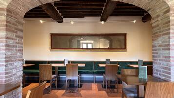 Restaurante com arcos de tijolo, mesas e cadeiras de madeira, e um espelho grande emoldurado na parede.
