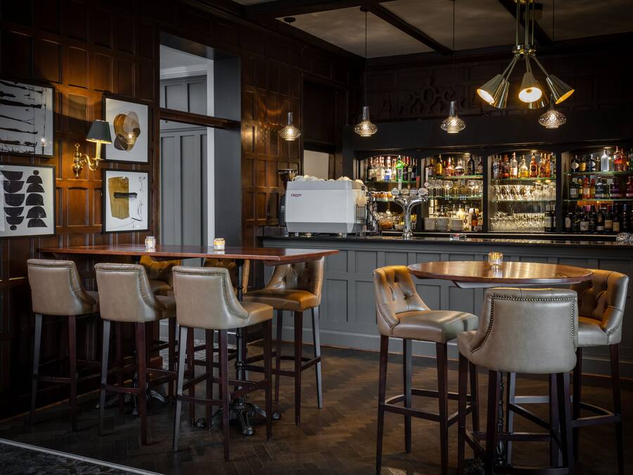 Uma área de bar com painéis de madeira, banquetas e uma máquina de café.