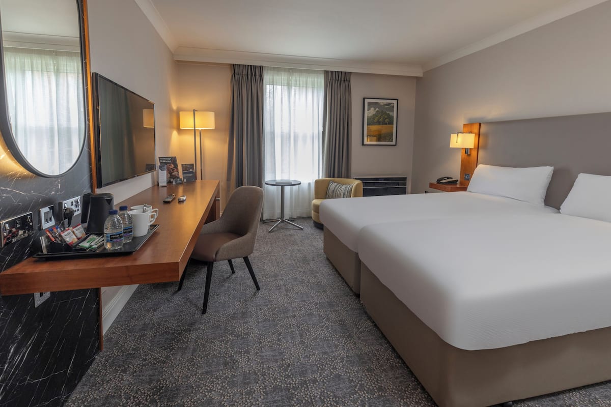 Quarto de hotel com uma cama grande, uma escrivaninha com cadeira, uma mesinha e um espelho.