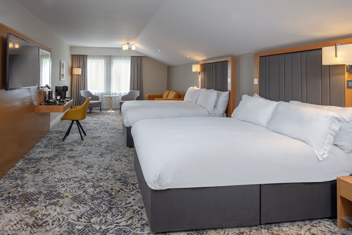 Quarto de hotel com uma cama grande, uma escrivaninha com cadeira, uma mesinha e uma televisão.